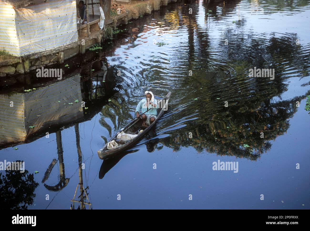 A fisherman rowing a sailboat using a stick in backwaters of kerala ...