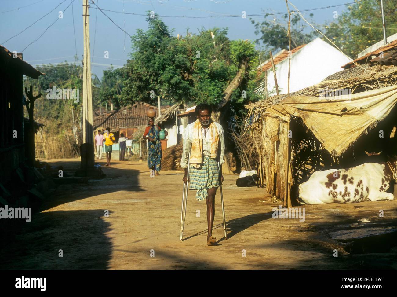 A handicapped man walking with sticks on the street of a village in ...
