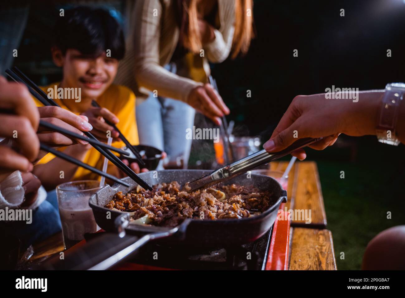 the group of people grilling the beef using the portable stove Stock ...