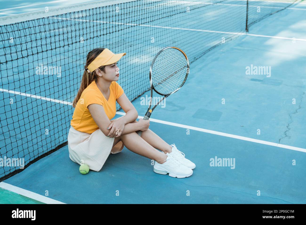 female tennis player sitting pensively holding racket on tennis court ...