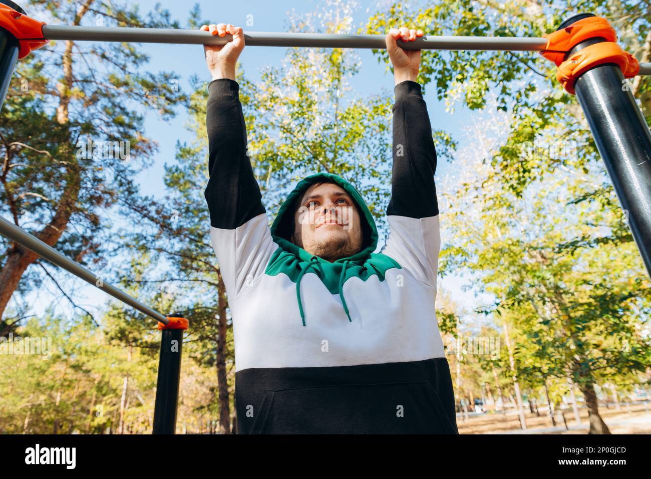 Male man hanging on bars on sunny autumn day. Outdoor park sports ...