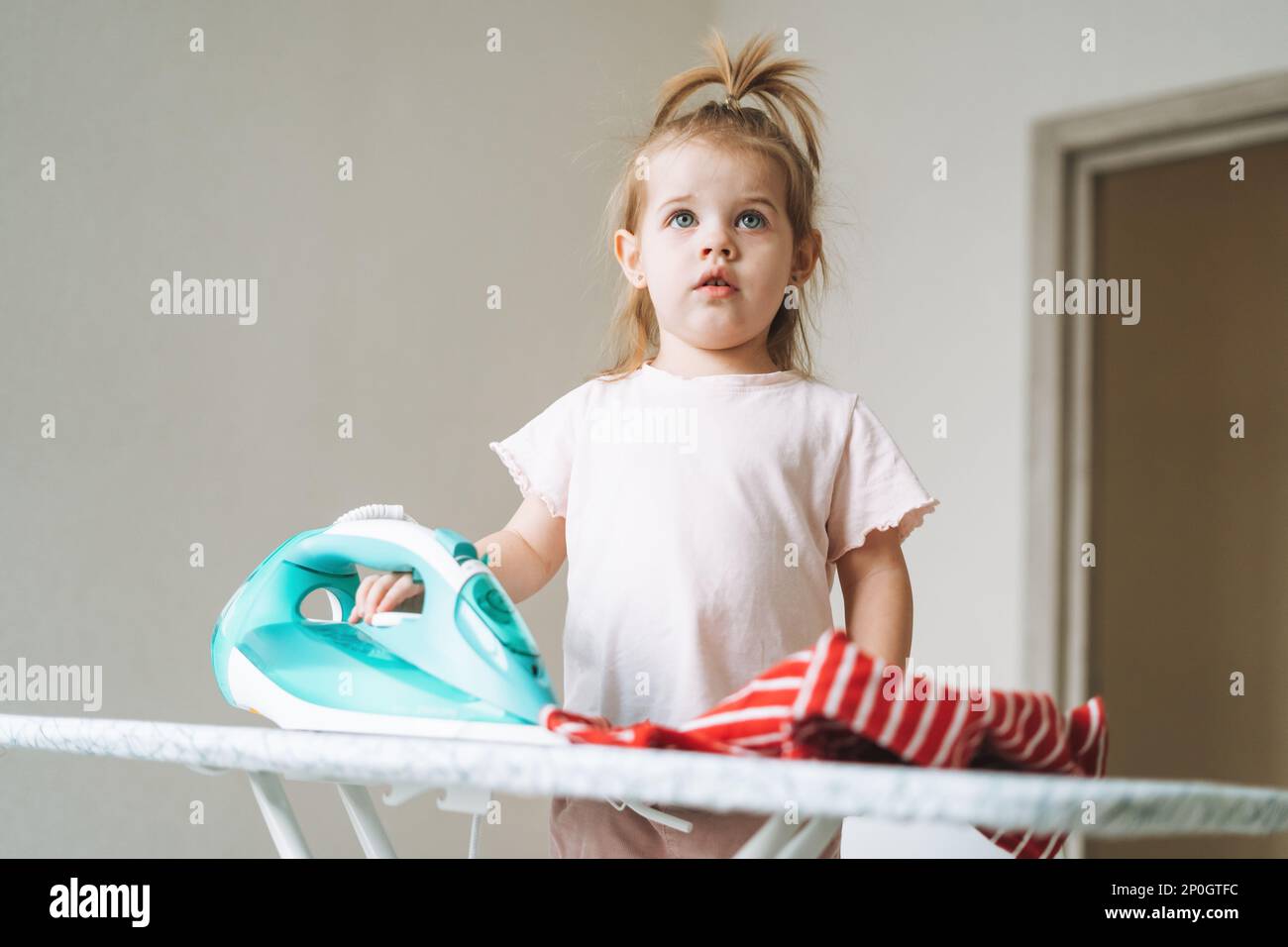 Cute little baby girl playing and ironing clothes with an iron at home ...