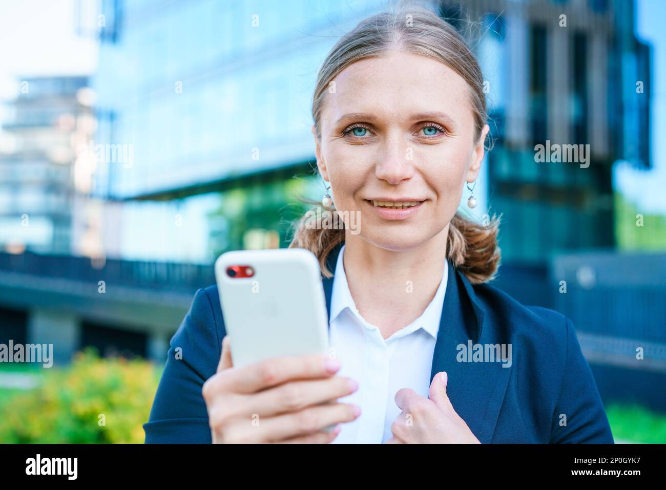 Successful female banker using smart phone outdoors while standing near ...