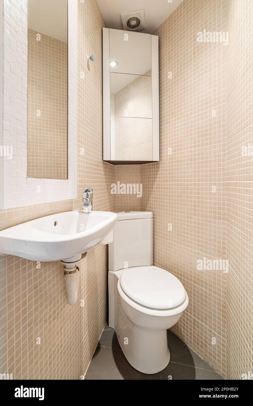 View of the toilet in the corner of compact tapered bathroom with beige ...