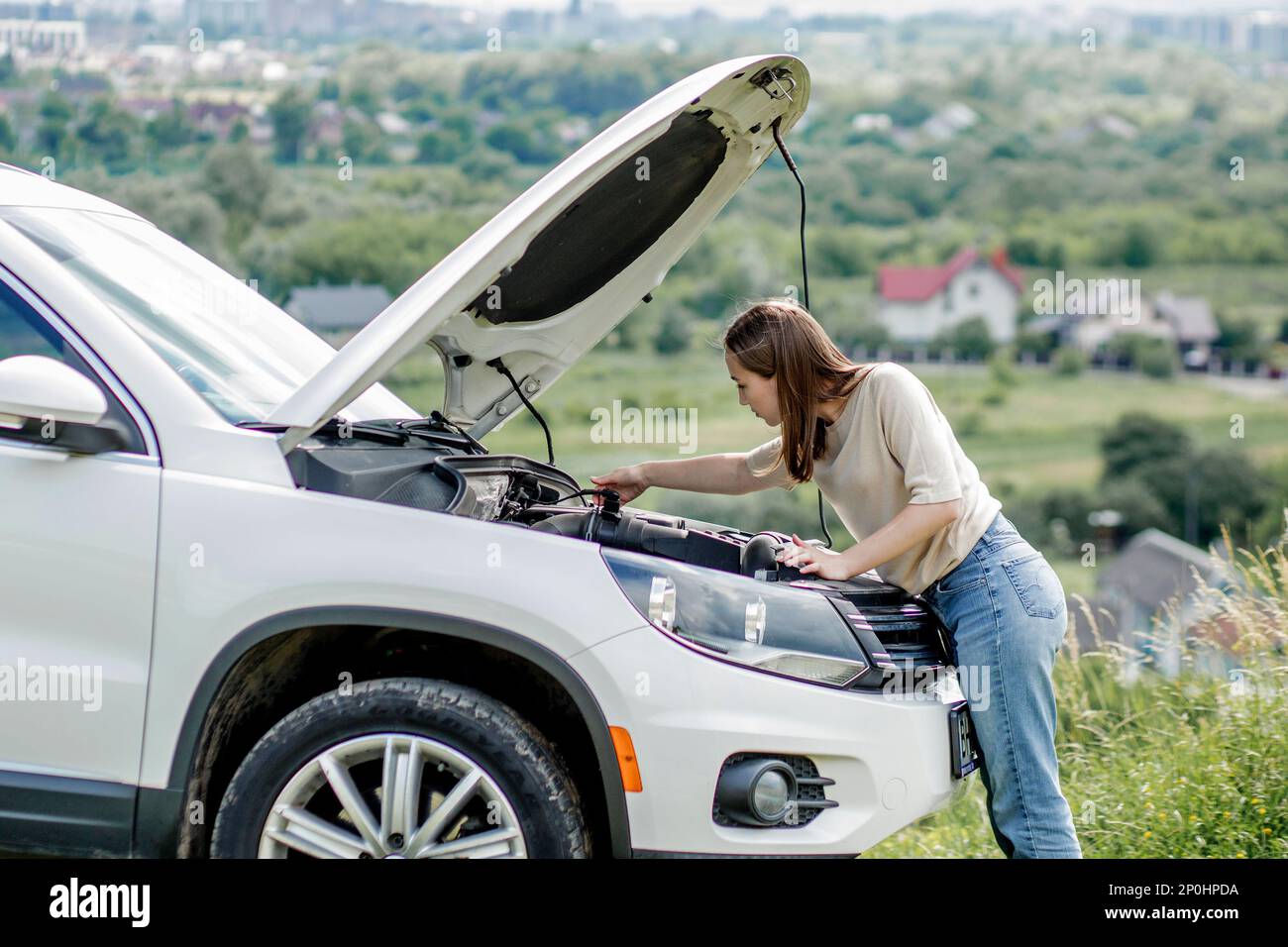 Confused female driver standing outside her car with the hood up and ...