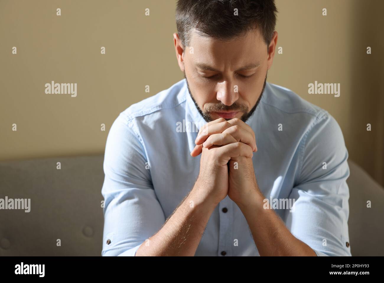Religious man with clasped hands praying indoors Stock Photo - Alamy