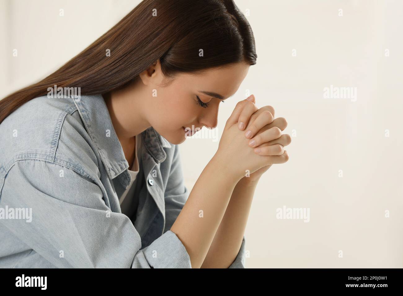 Religious young woman with clasped hands praying indoors, closeup Stock ...