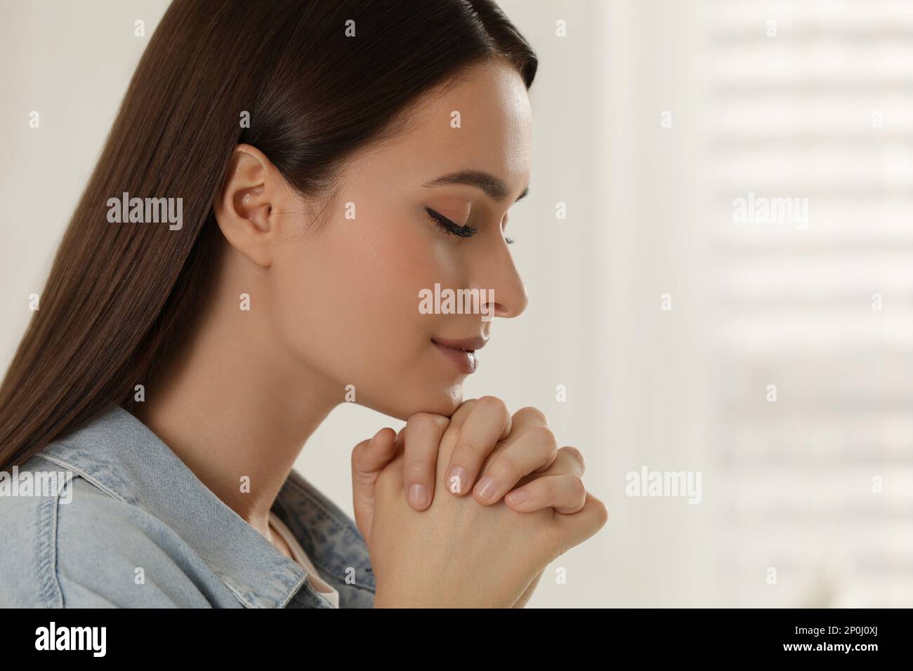 Religious young woman with clasped hands praying indoors, closeup Stock ...