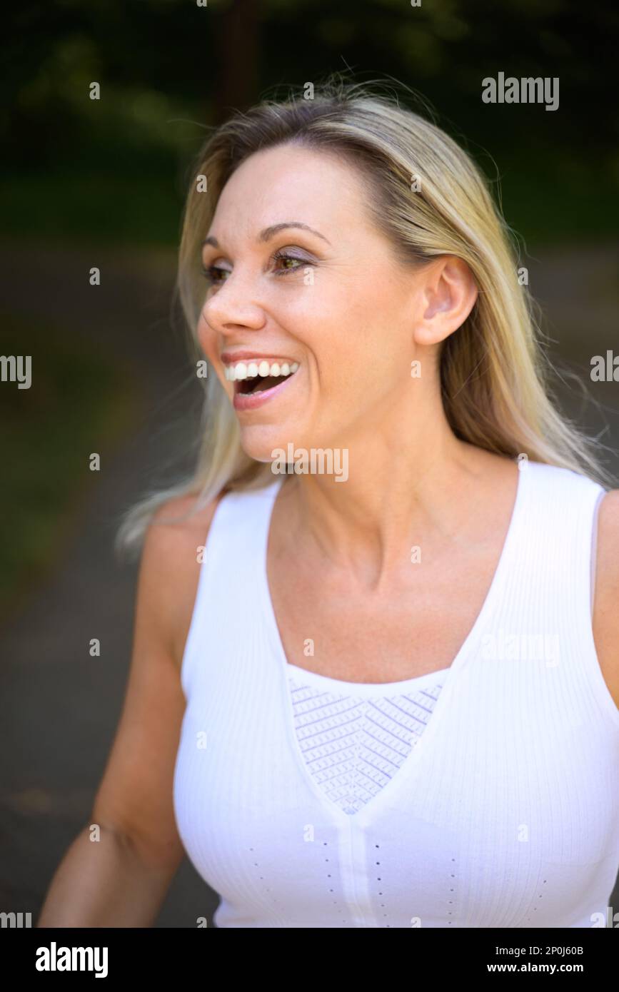 Cute vivacious blond middle aged woman outdoors laughing happily as she looks to the side Stock ...
