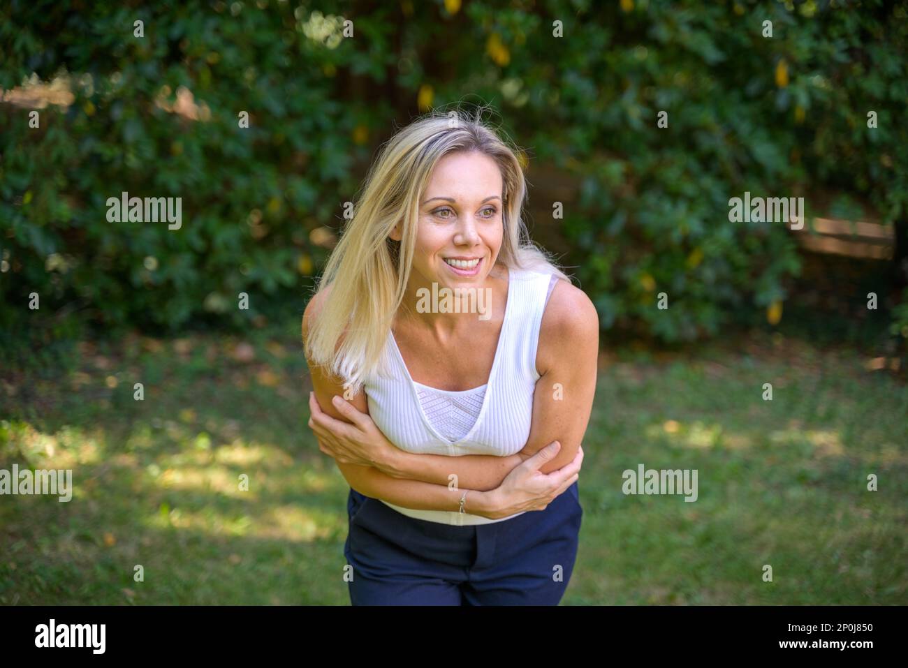 Blond woman leaning to the camera as she clasps her chest looking aside ...