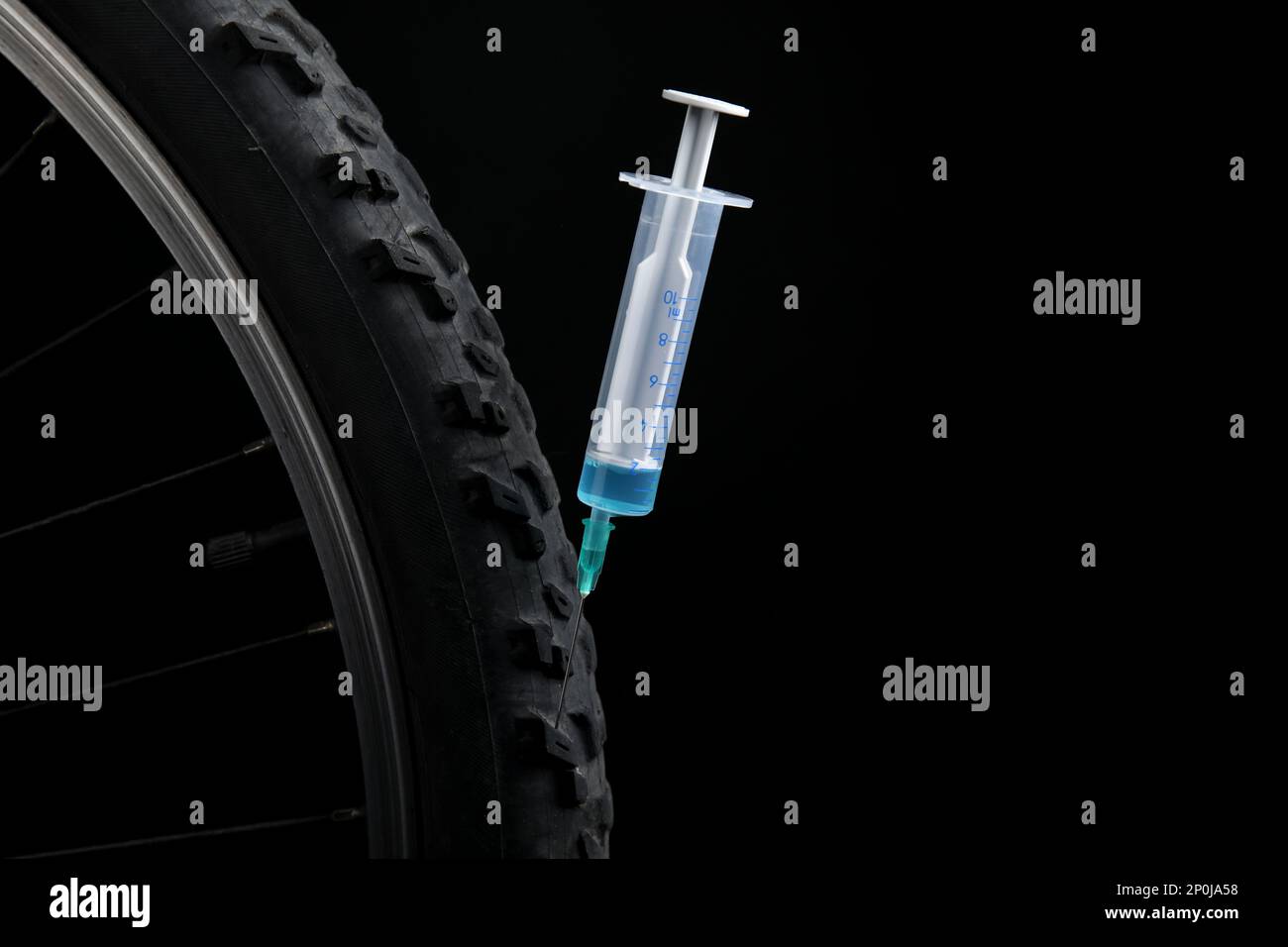 Bike wheel with syringe on black background, closeup. Using doping in ...