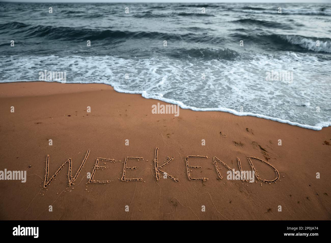 Sea wave rolling onto sandy beach with written word Weekend Stock Photo ...