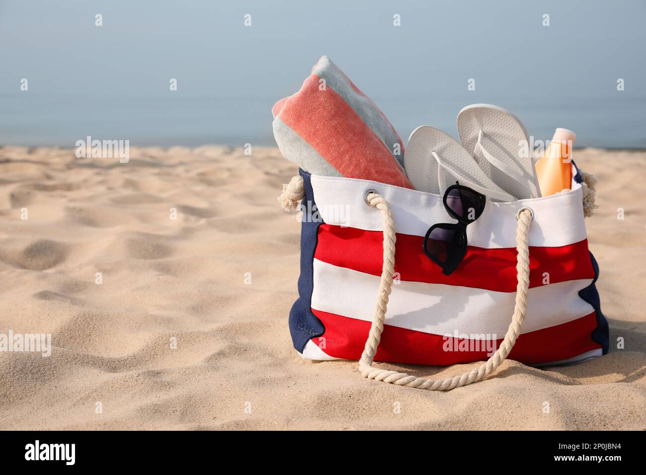 Beach bag with flip flops, towel, sunglasses and sunscreen on sandy ...
