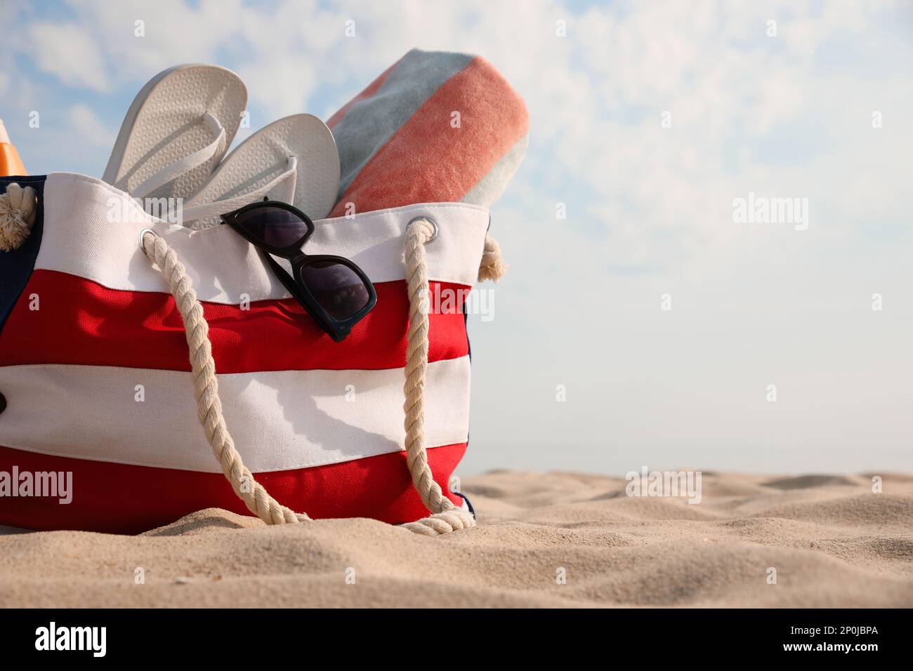 Beach bag with flip flops, towel and sunglasses on sand, space for text ...