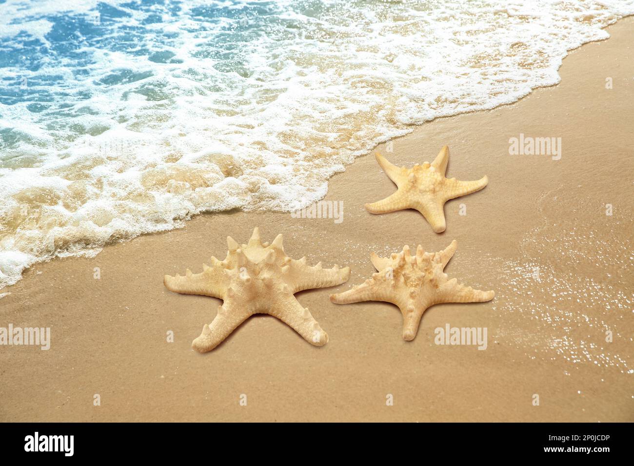 Beautiful waves and sea stars on sandy beach Stock Photo - Alamy