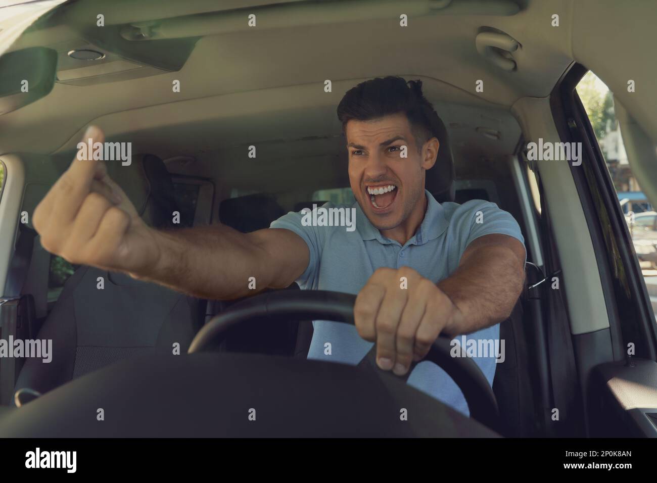 Stressed angry man showing middle finger in modern car, view through ...