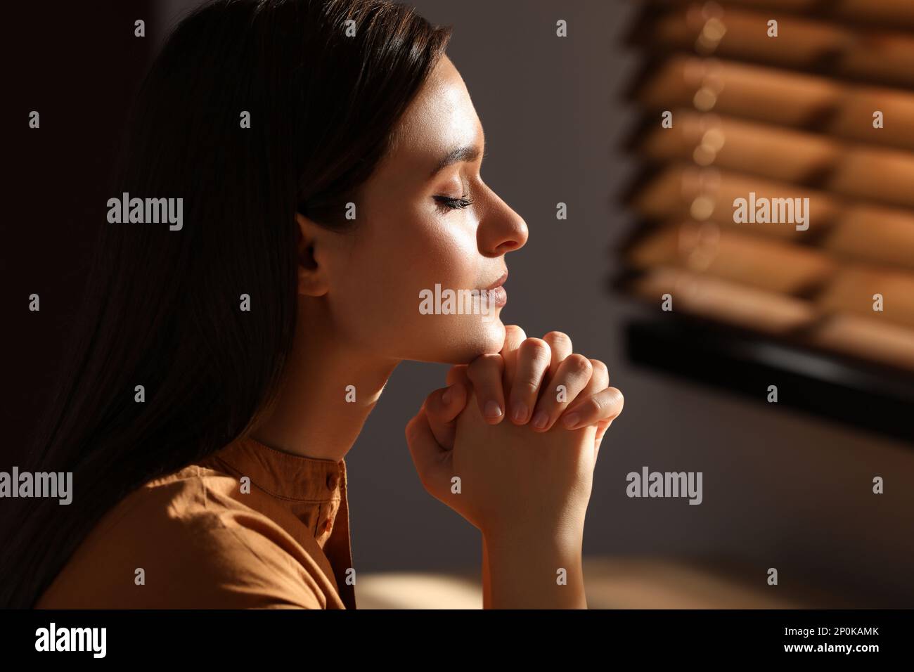Religious young woman with clasped hands praying indoors Stock Photo ...