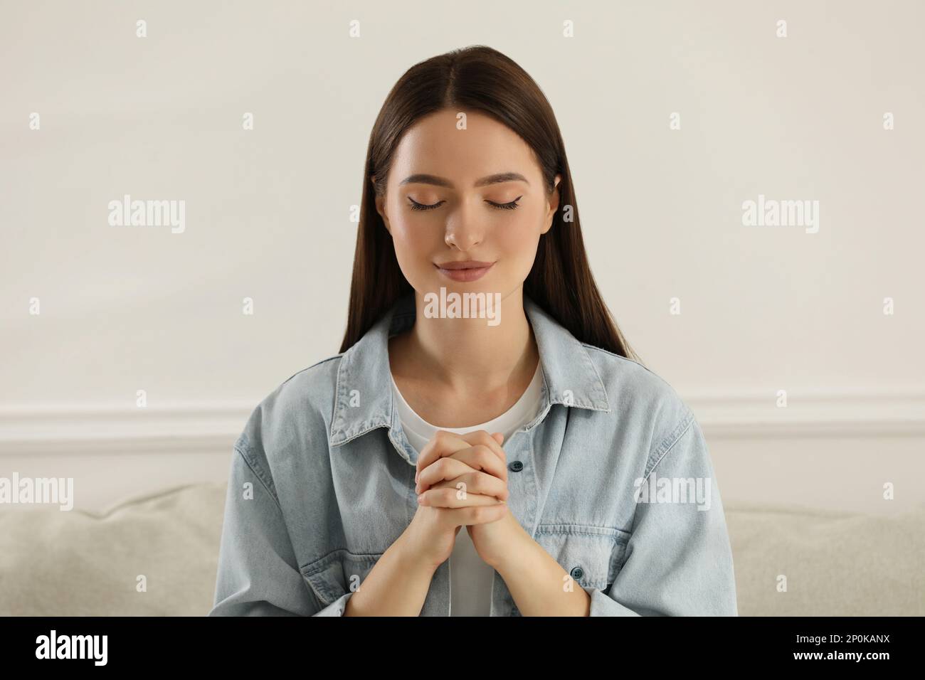 Religious young woman with clasped hands praying indoors Stock Photo ...