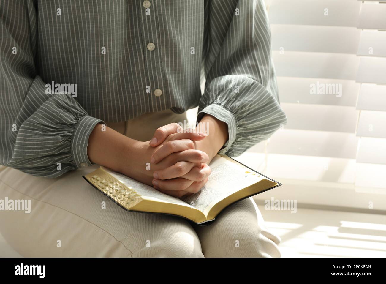 Religious woman praying over Bible near window indoors, closeup Stock ...