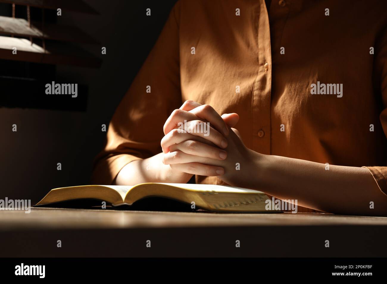 Religious woman praying over Bible at wooden table indoors, closeup ...