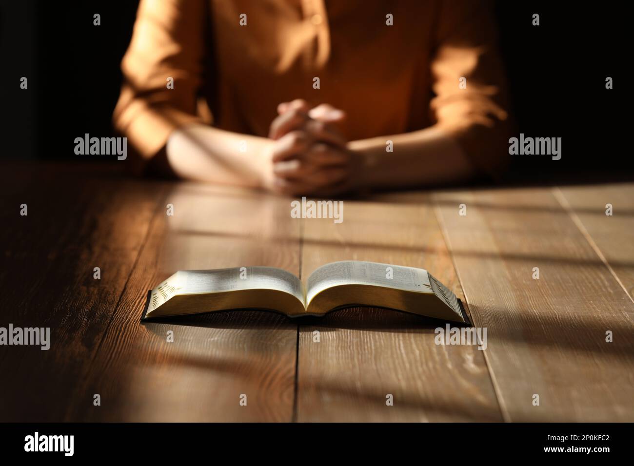 Religious woman praying over Bible at wooden table indoors, focus on ...