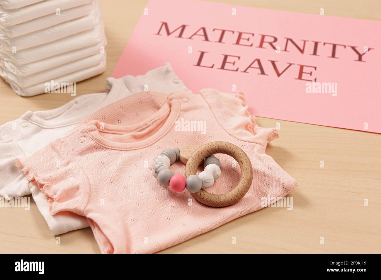 Baby clothes, toy, diapers and note with text Maternity Leave on wooden ...
