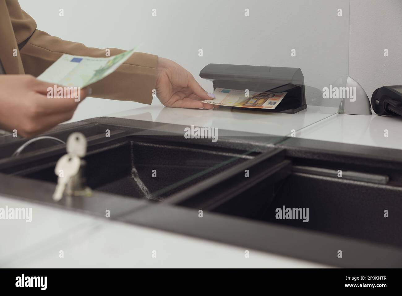 Cashier checking money with currency detector at exchange department ...