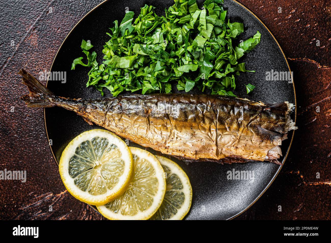 Grilled Mackerel Scomber fish on a plate with greens and lemon. Dark ...