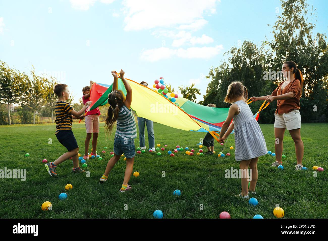 Group of children and teacher playing with rainbow playground parachute ...