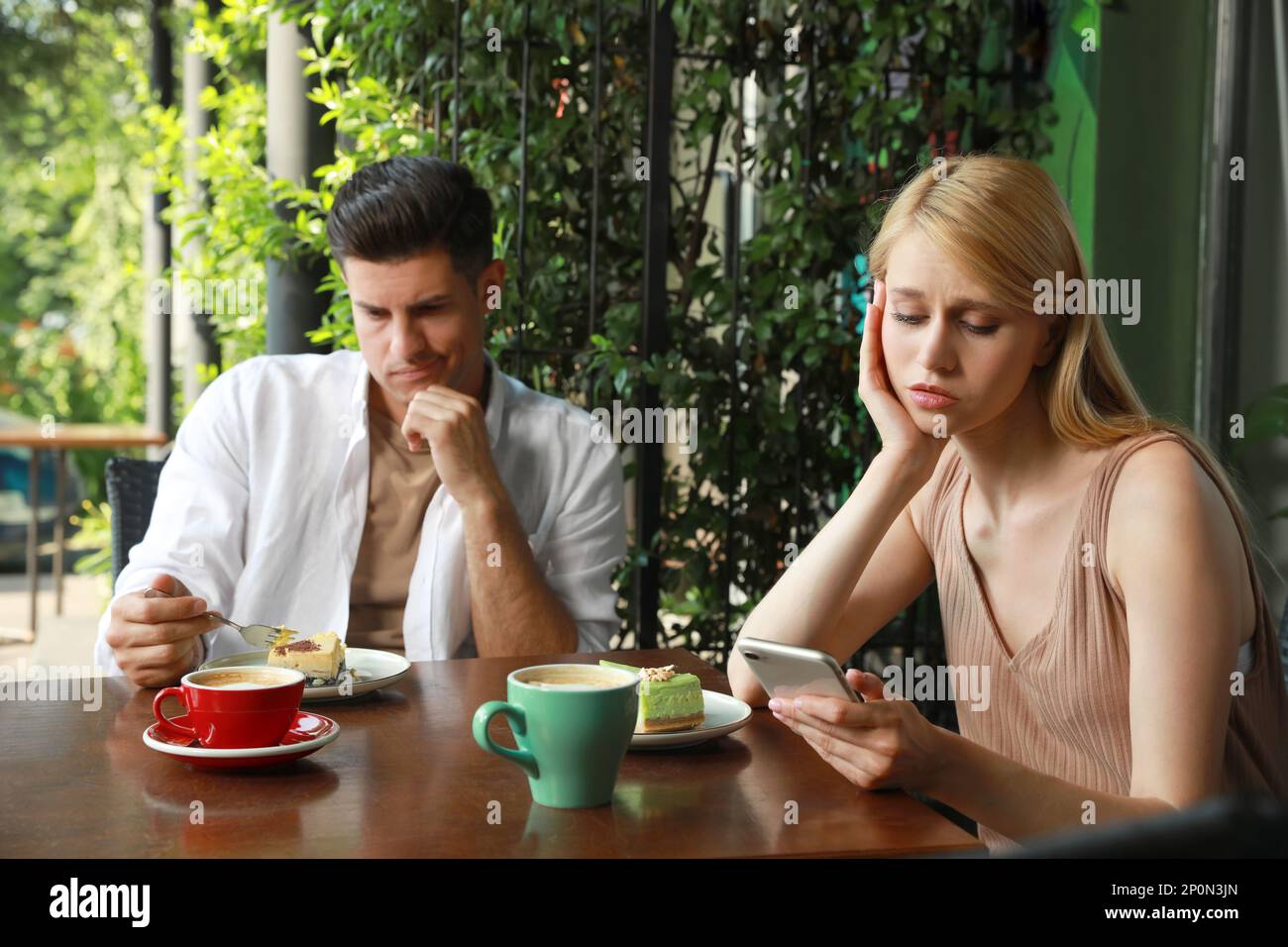 Young woman with smartphone ignoring her boyfriend in outdoor cafe ...