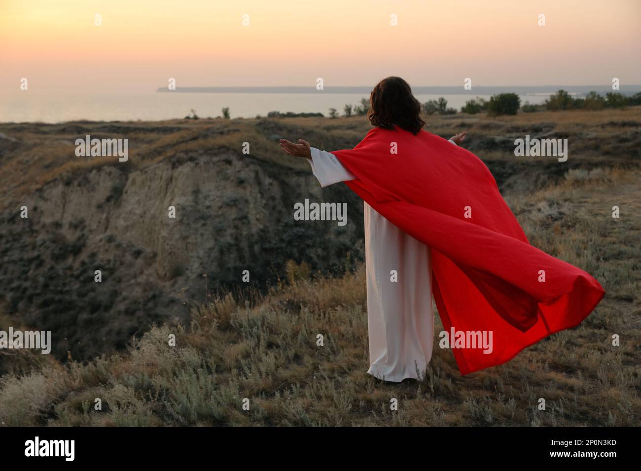 Jesus Christ raising hands on hills at sunset, back view. Space for ...