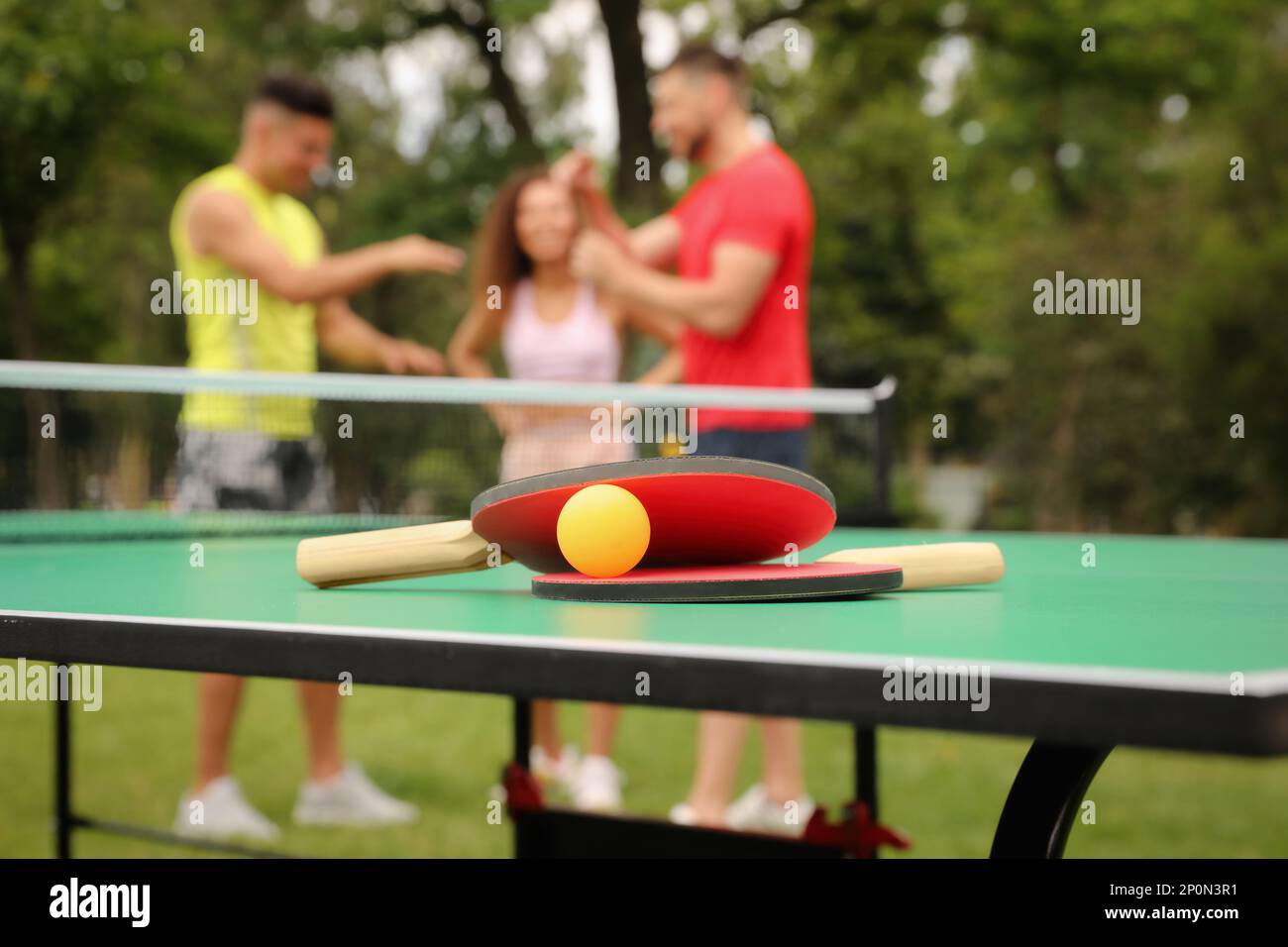 Friends talking near ping pong table outdoors, focus on rackets and ...