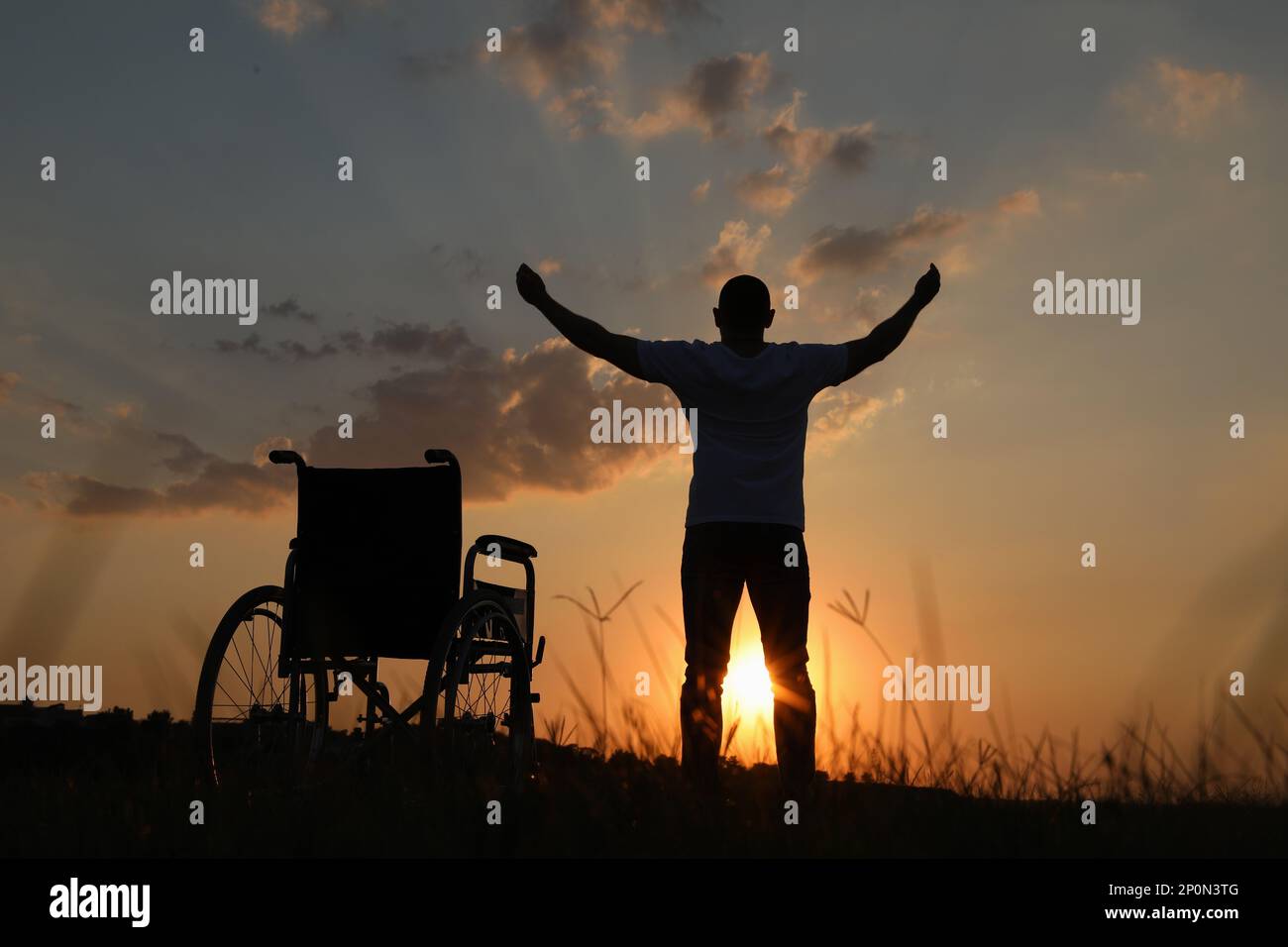 Man raising hands up to sky near wheelchair at sunset, back view ...