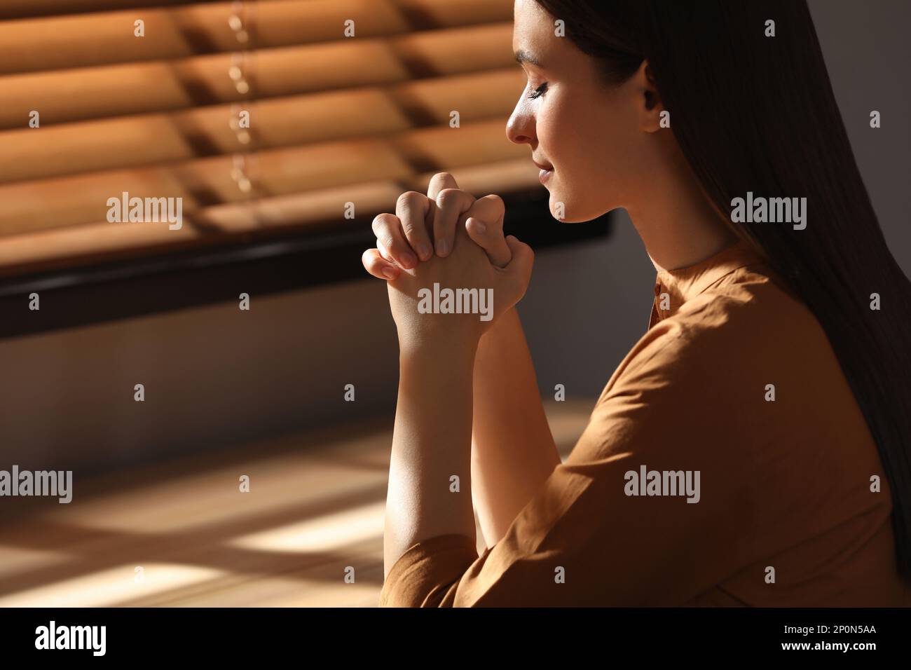 Religious young woman with clasped hands praying indoors Stock Photo ...