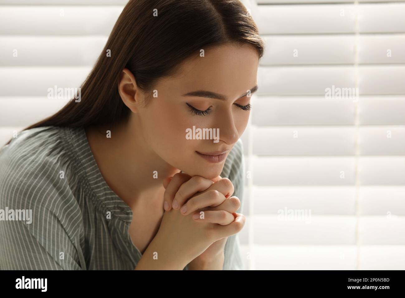 Religious young woman praying near window indoors, closeup Stock Photo - Alamy