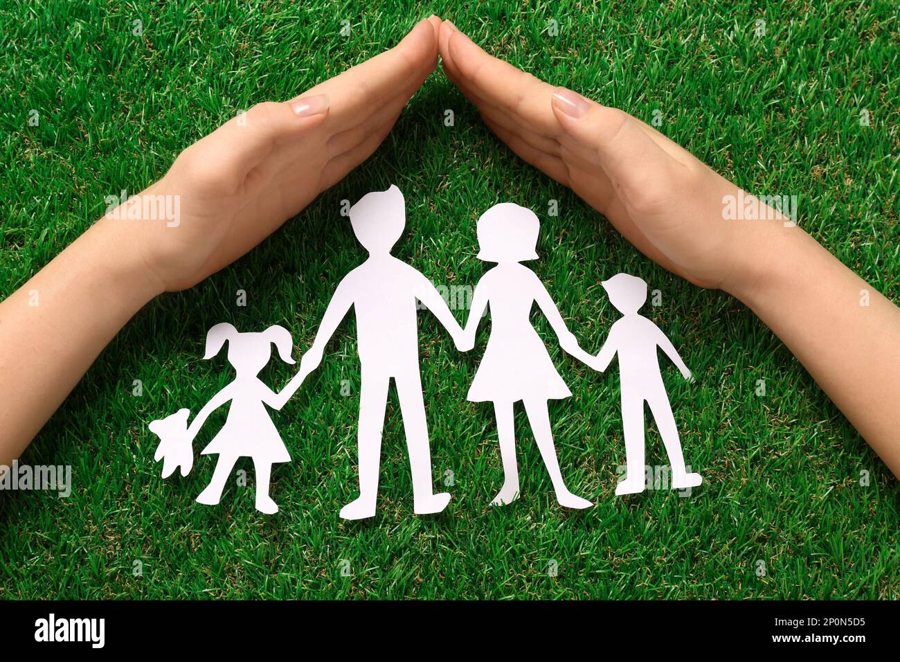 Woman covering family paper cutout with hands on green grass, top view ...