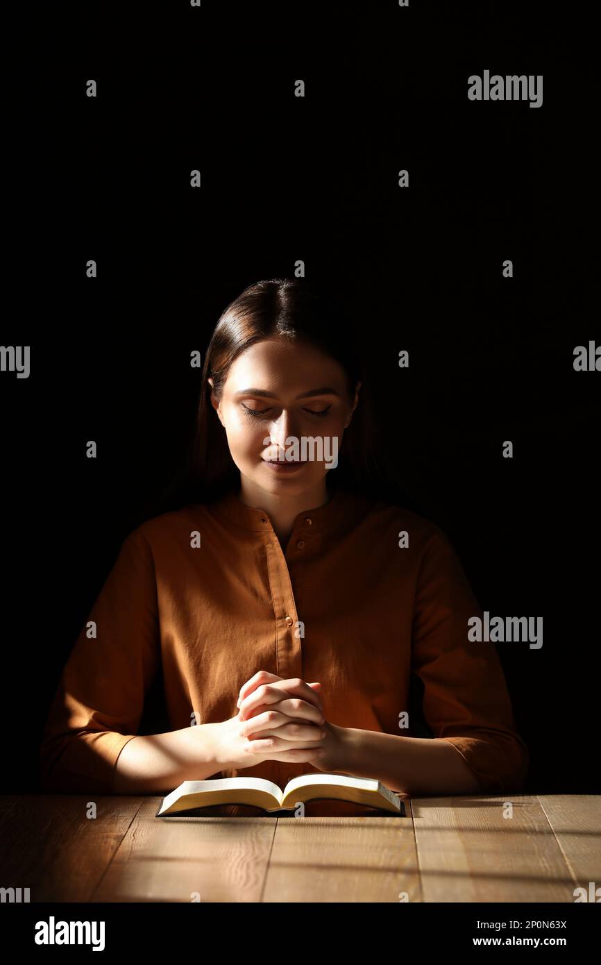 Religious young woman praying over Bible at wooden table indoors Stock ...