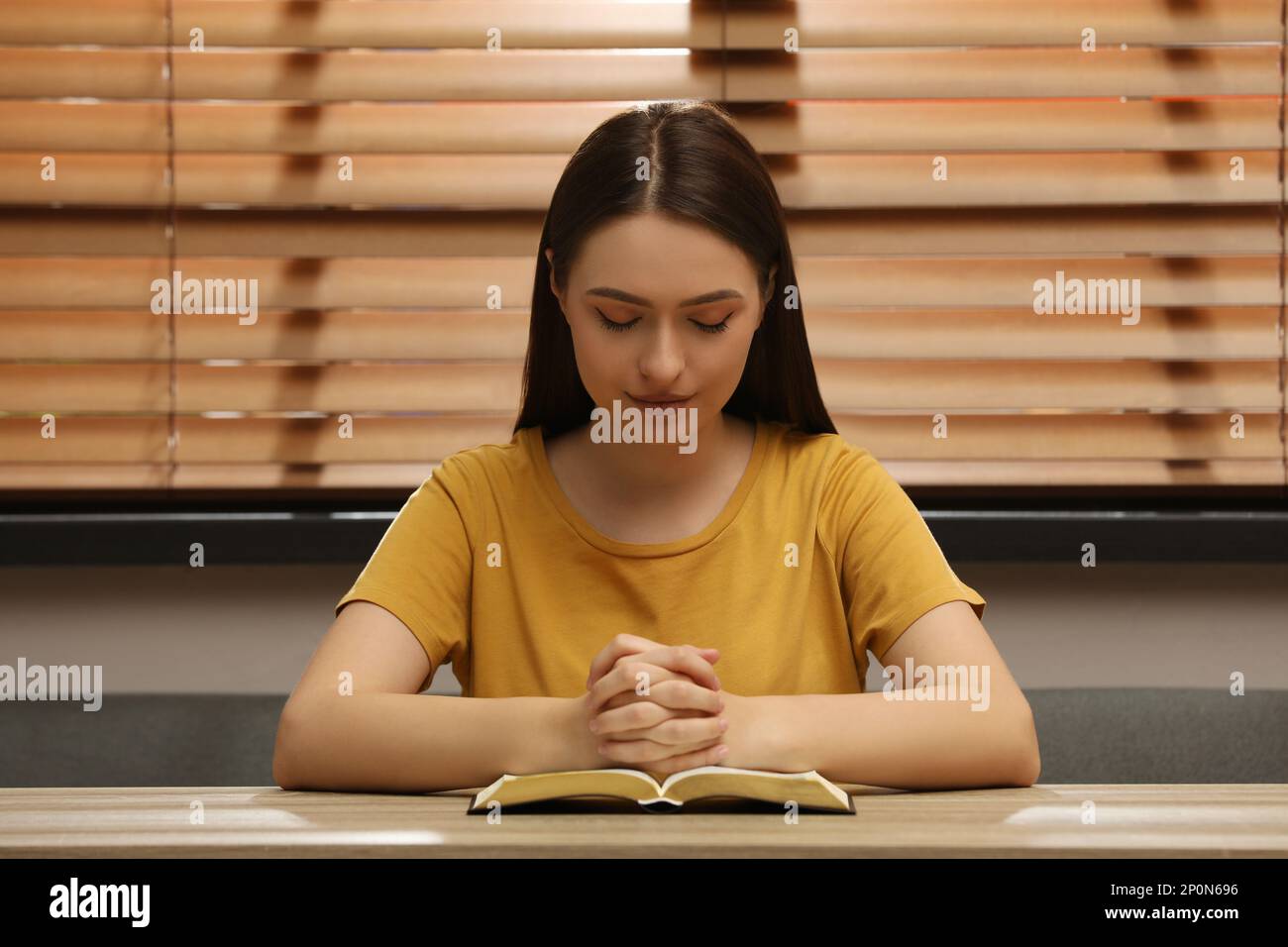 Religious young woman praying over Bible at wooden table indoors Stock ...
