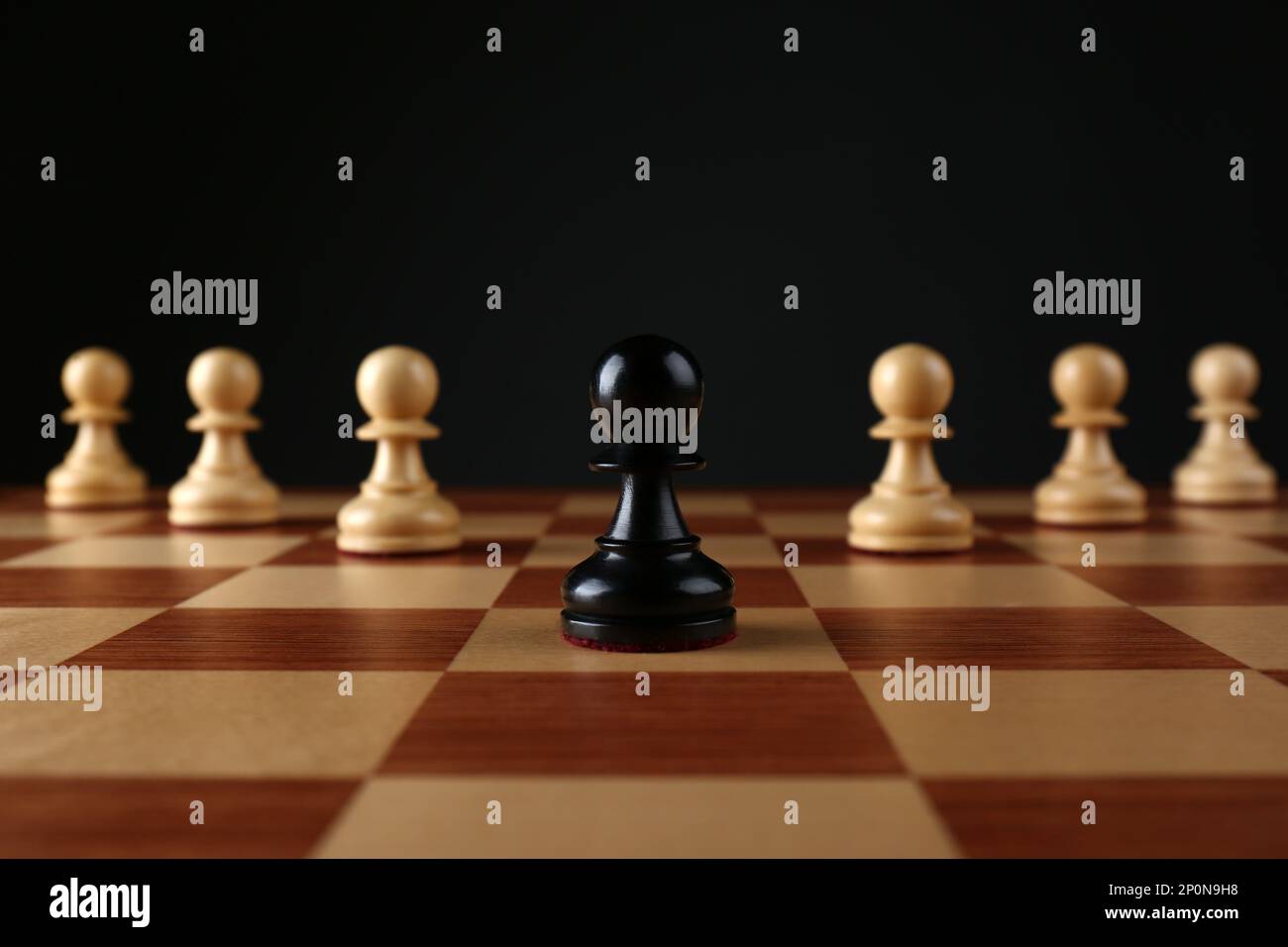 Black pawn in front of white ones on wooden chess board against dark ...