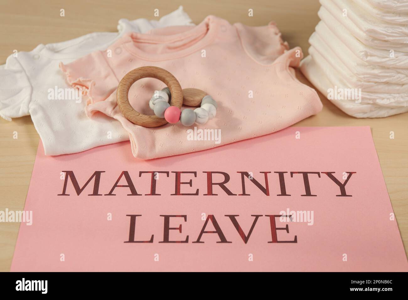 Baby clothes, toy, diapers and note with text Maternity Leave on wooden ...