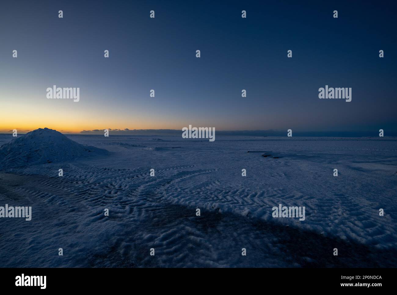Road and flat snowy landscape in almost darkness with tire tracks going ...