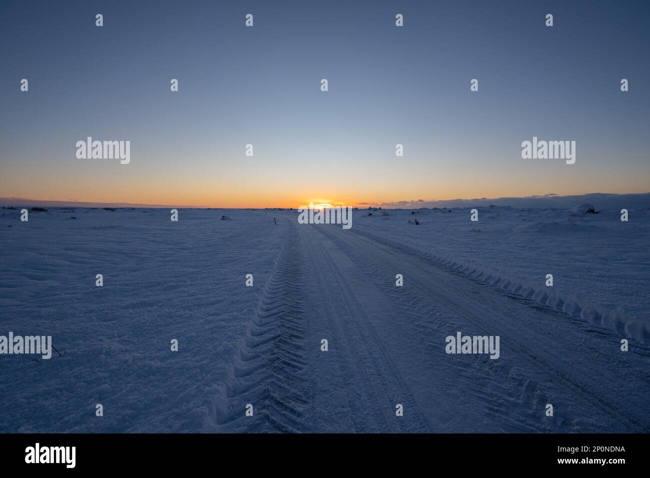 Road and flat snowy landscape in almost darkness with tire tracks going ...