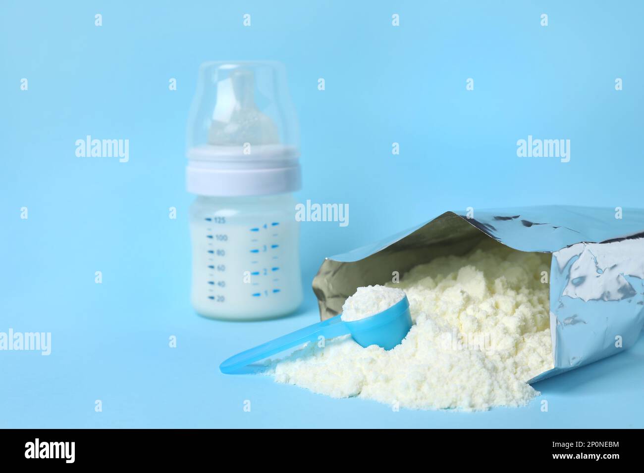 Bag of powdered infant formula, feeding bottle and scoop on light blue ...