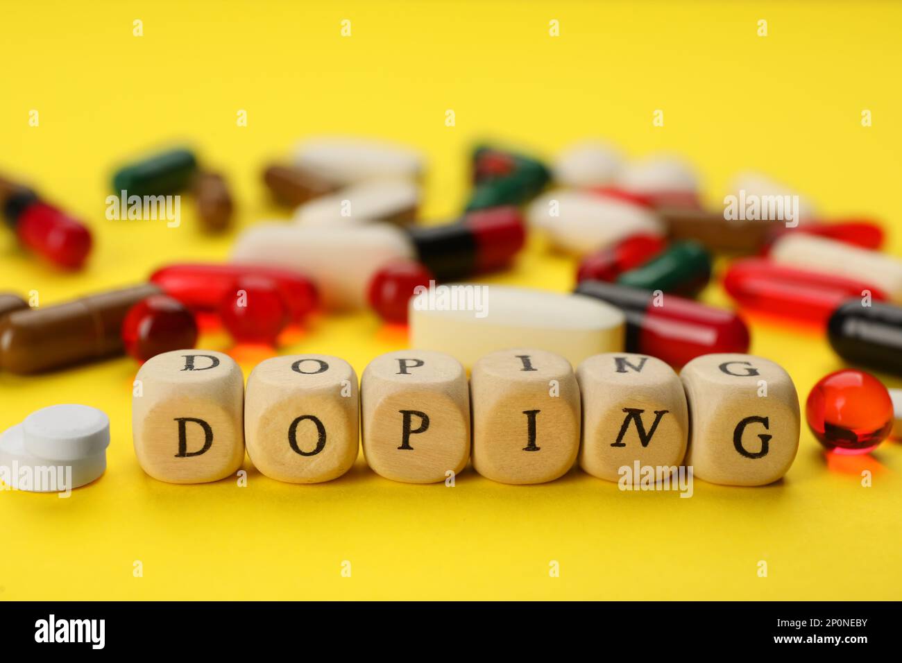 Wooden cubes with word Doping and drugs on yellow background, closeup ...