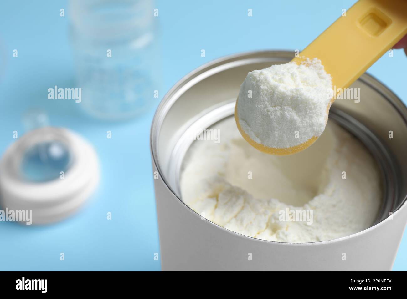 Scoop of powdered infant formula over can on light blue background ...