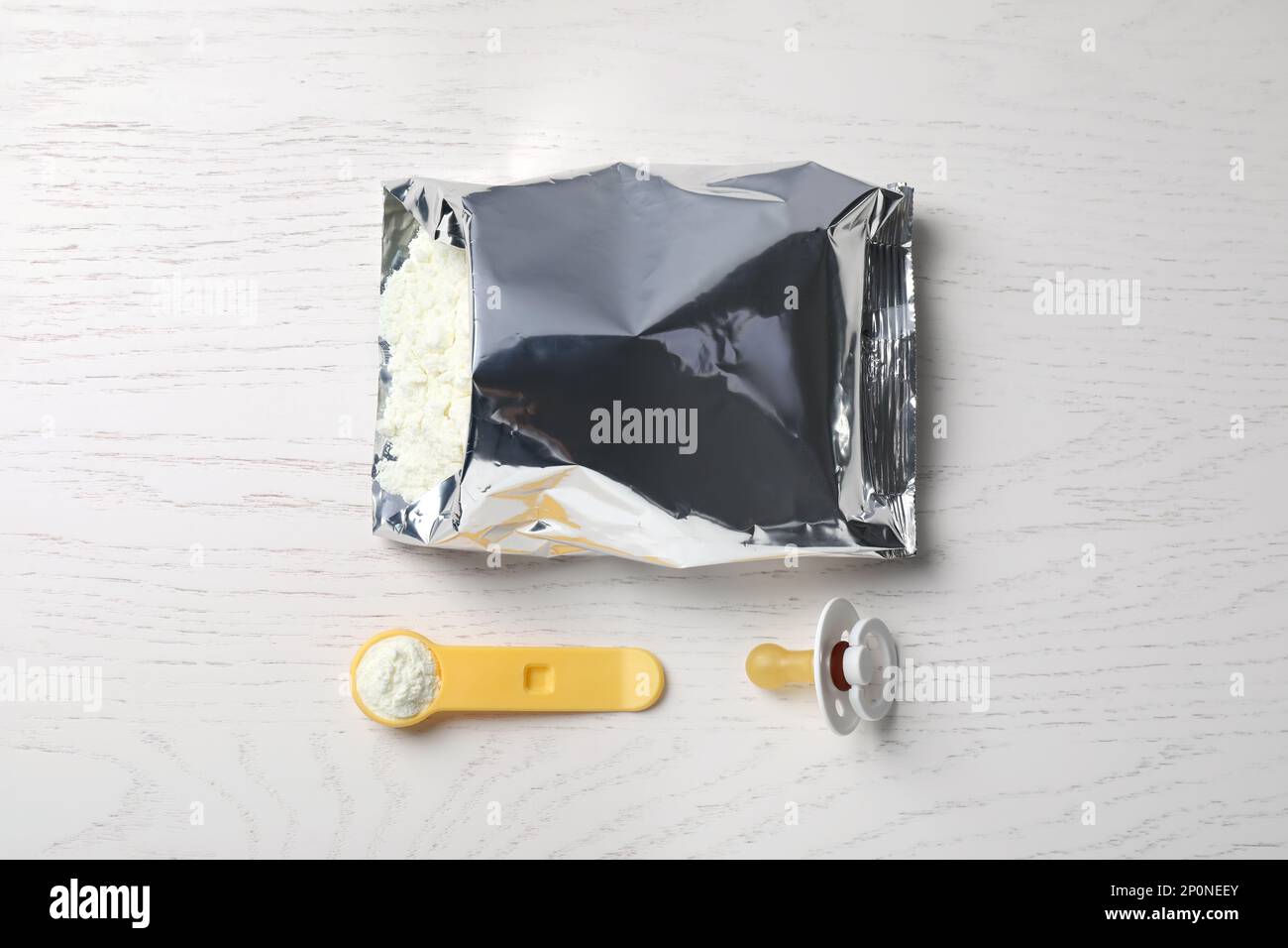 Bag of powdered infant formula, scoop and pacifier on white wooden ...