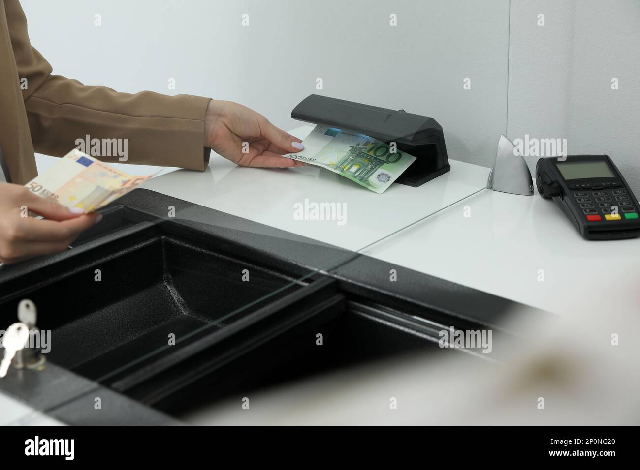 Cashier checking money with detector at currency exchange department in ...