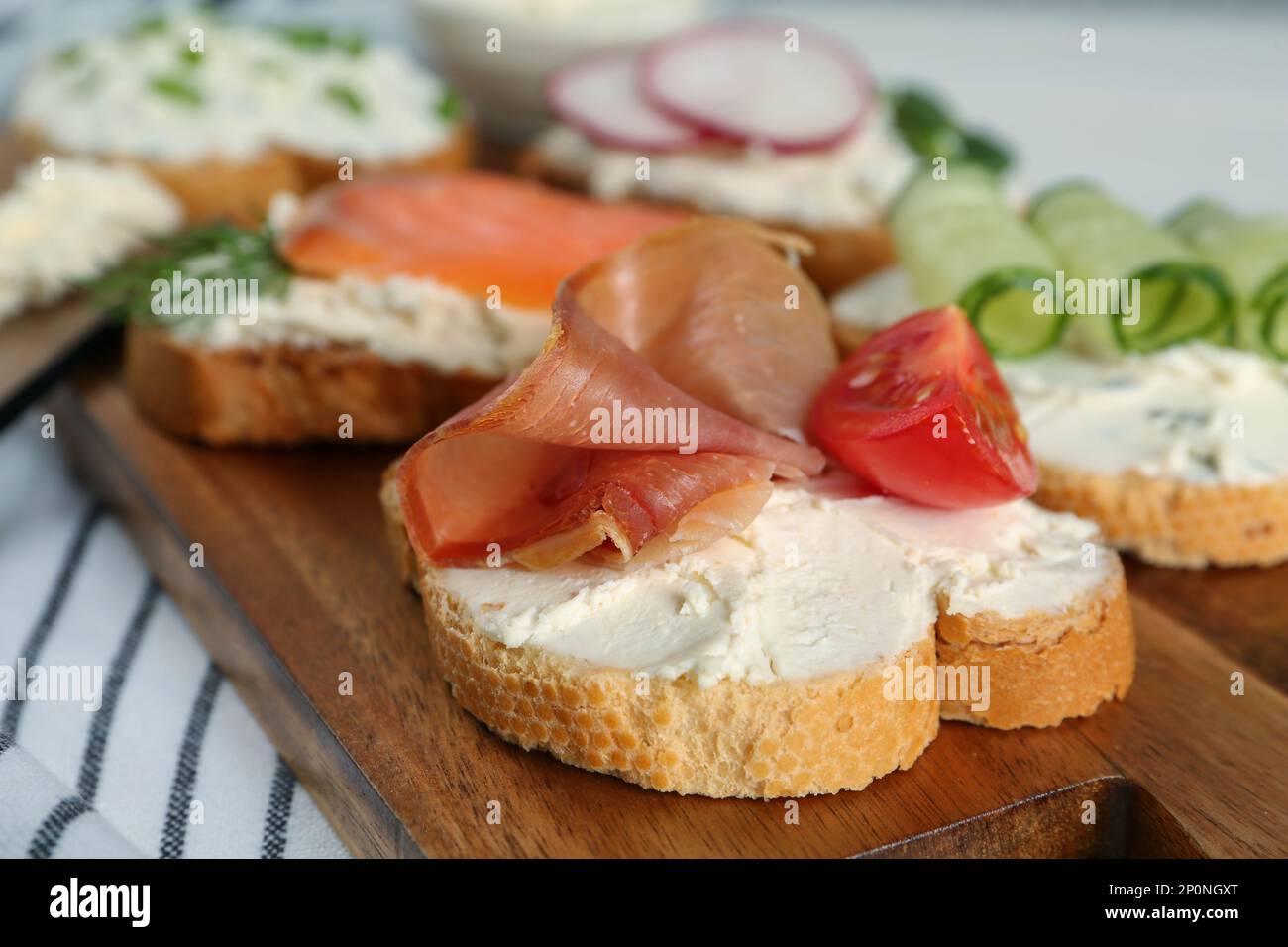 Toasted bread with cream cheese and different toppings on wooden board ...