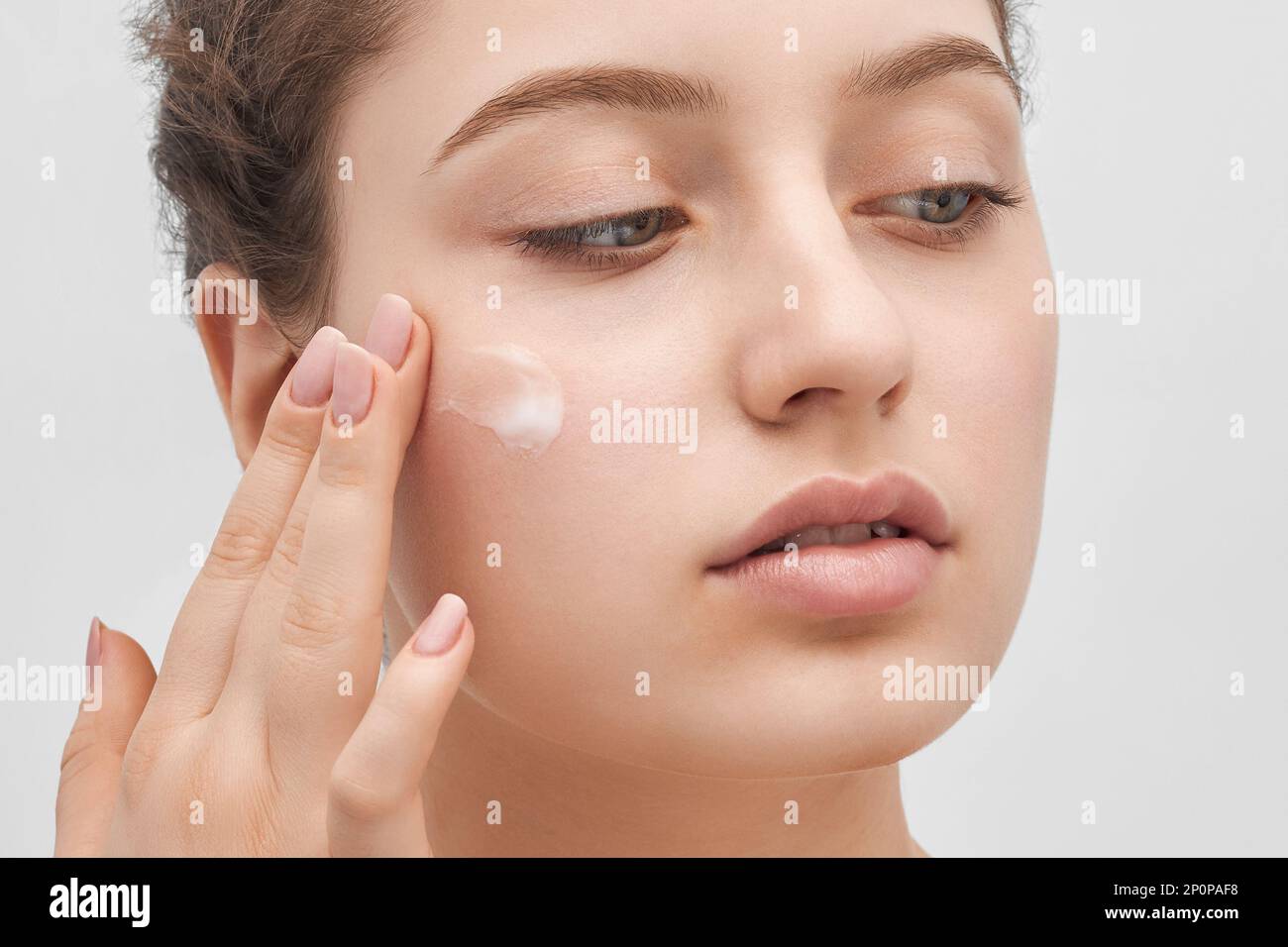 Young beautiful girl applies cream to her face, close-up. Long hair ...
