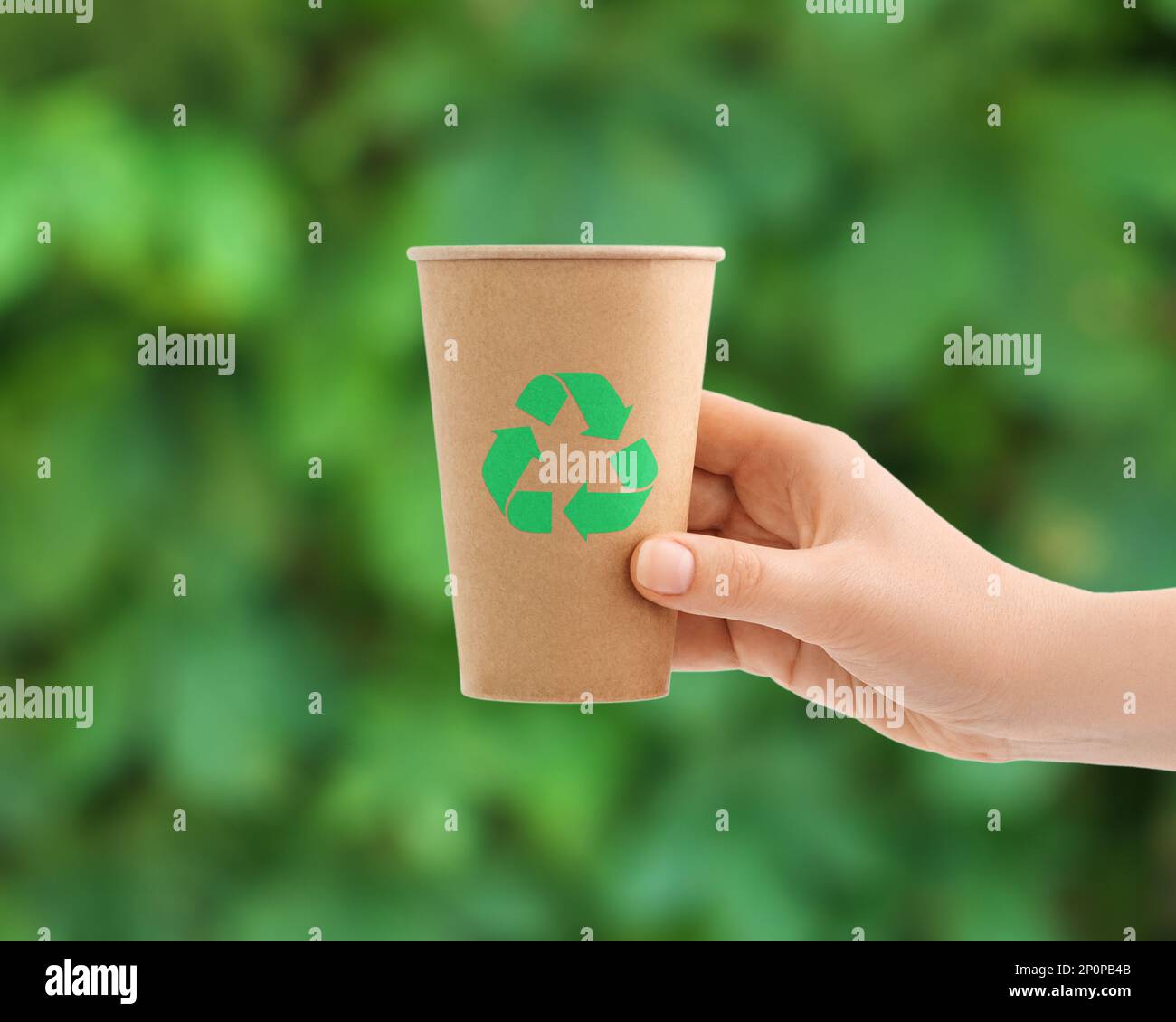 Disposable paper cup with recycle sign in a female hand against blurred ...